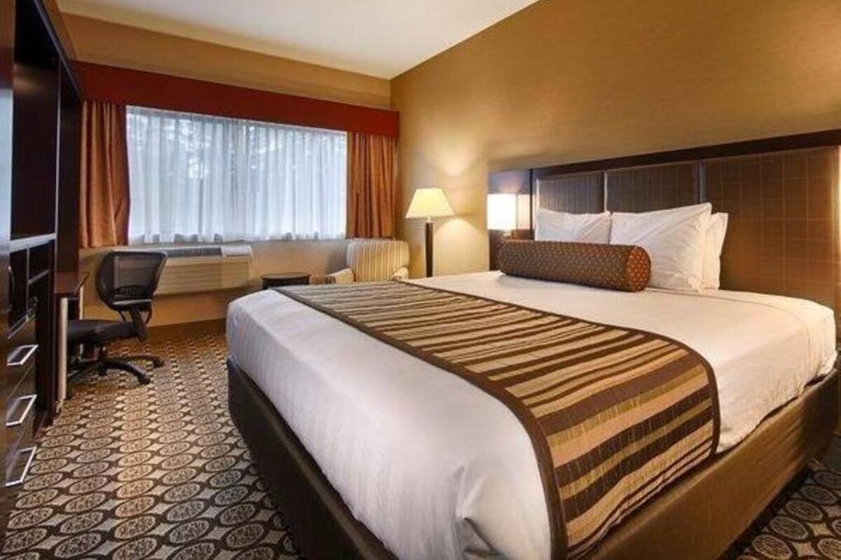 Quarto de hotel com uma cama grande, uma escrivaninha, uma cadeira e uma janela com cortinas.