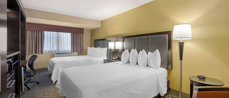 Quarto de hotel com duas camas, uma mesa, uma cadeira, uma luminária e uma janela com cortinas.