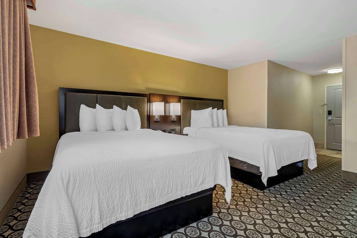 Quarto de hotel com duas camas, piso estampado e esquema de cores neutras.