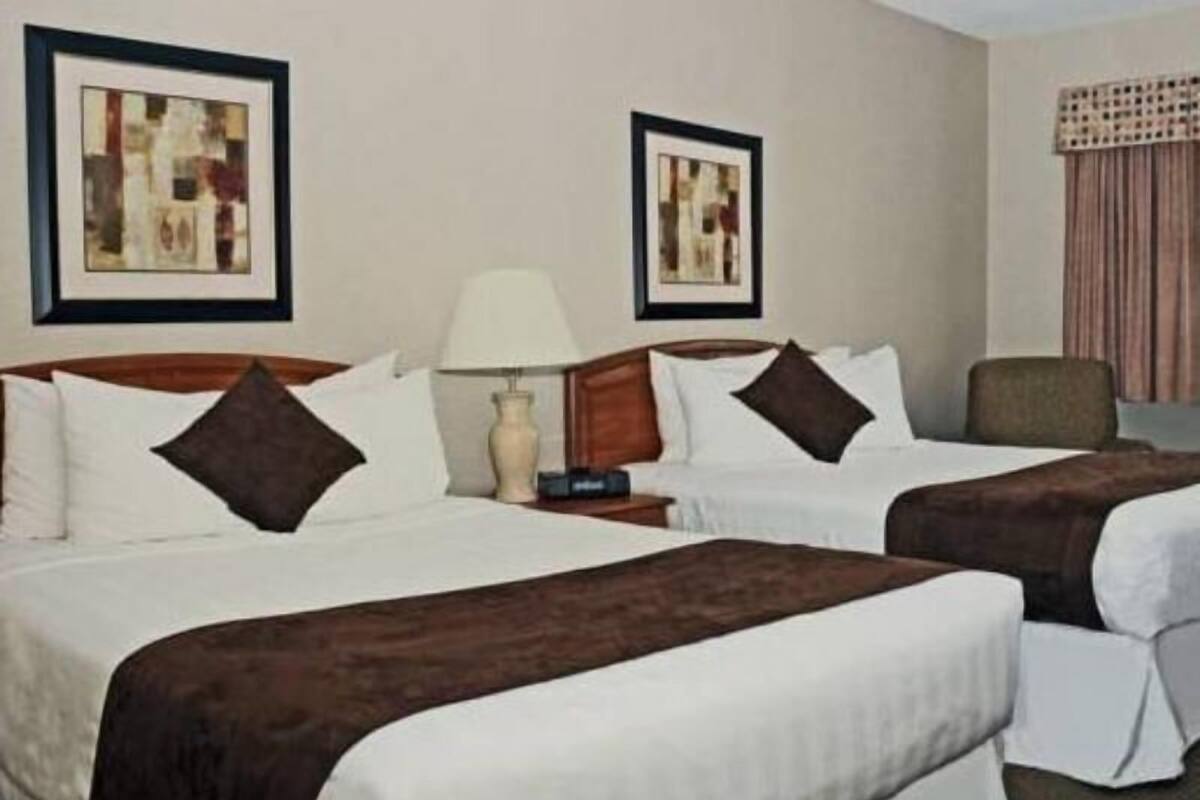 Quarto de hotel com duas camas, uma mesa de cabeceira com abajur e duas imagens emolduradas na parede.