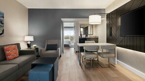 Quarto de hotel moderno com área de estar, espaço para refeições e uma televisão grande.