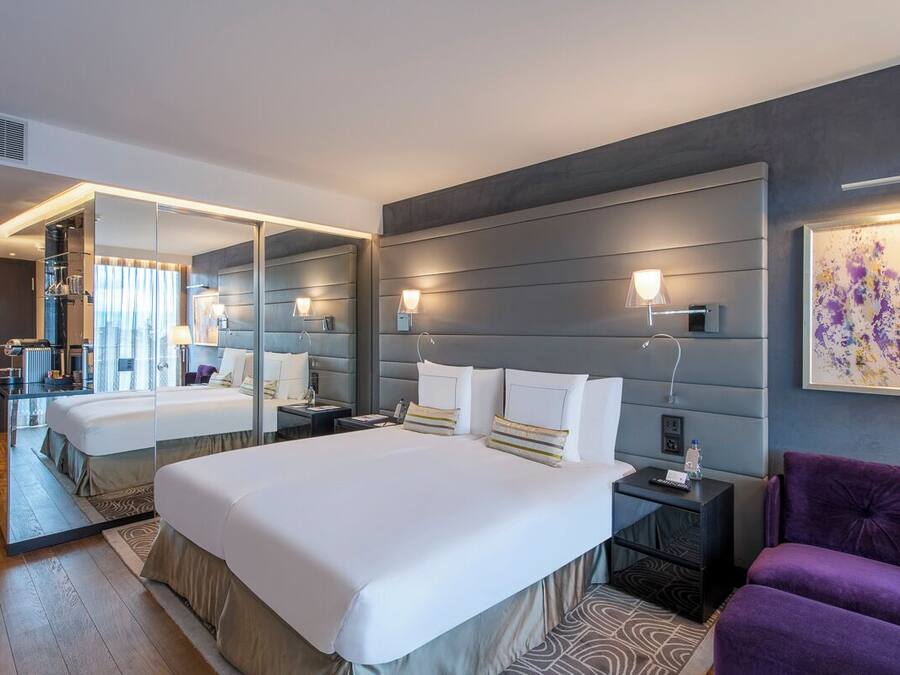 Quarto de hotel moderno com uma cama grande, espaço de estar e espelho.