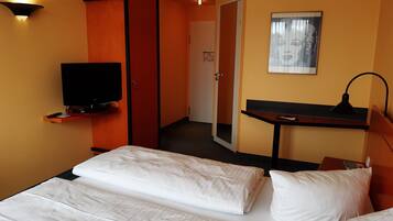 Quarto de hotel com cama, televisão, escrivaninha e porta.