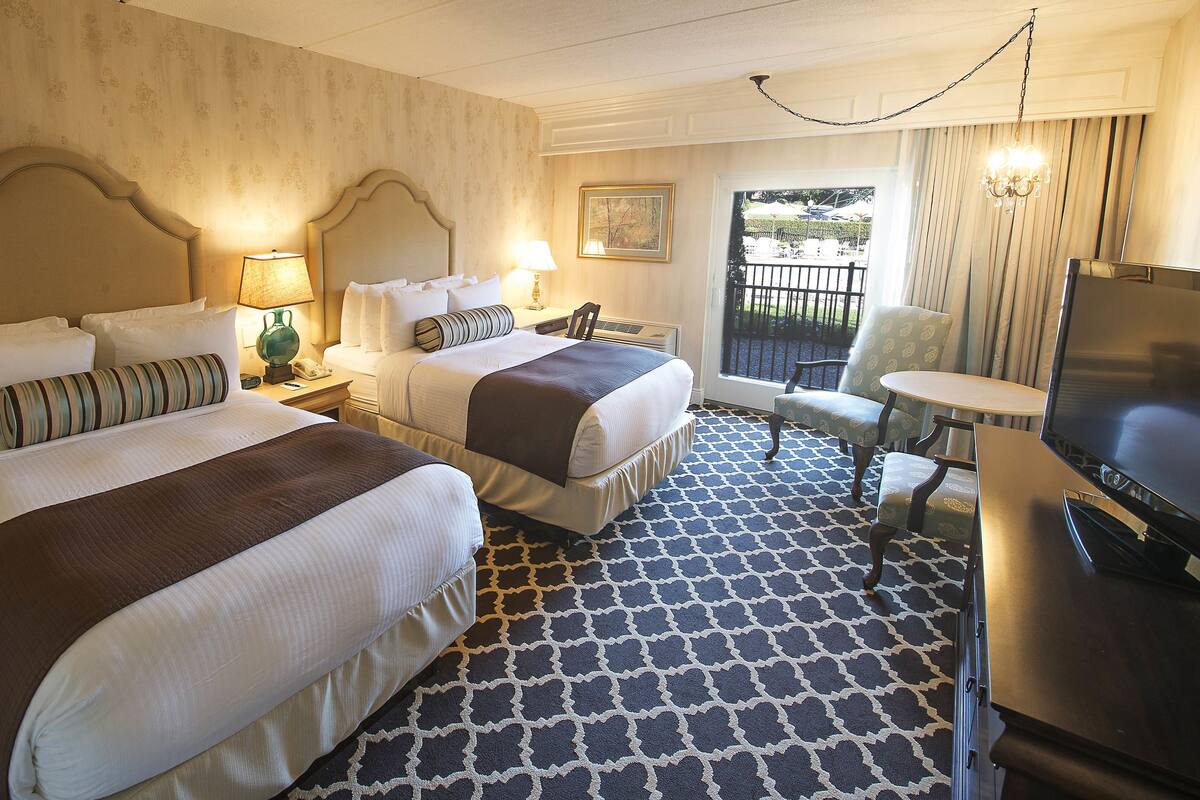 Quarto de hotel com duas camas, televisão, uma cadeira e varanda com vista.