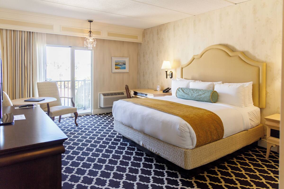 Quarto de hotel com uma cama grande, uma mesa, uma cadeira e vista para o exterior.
