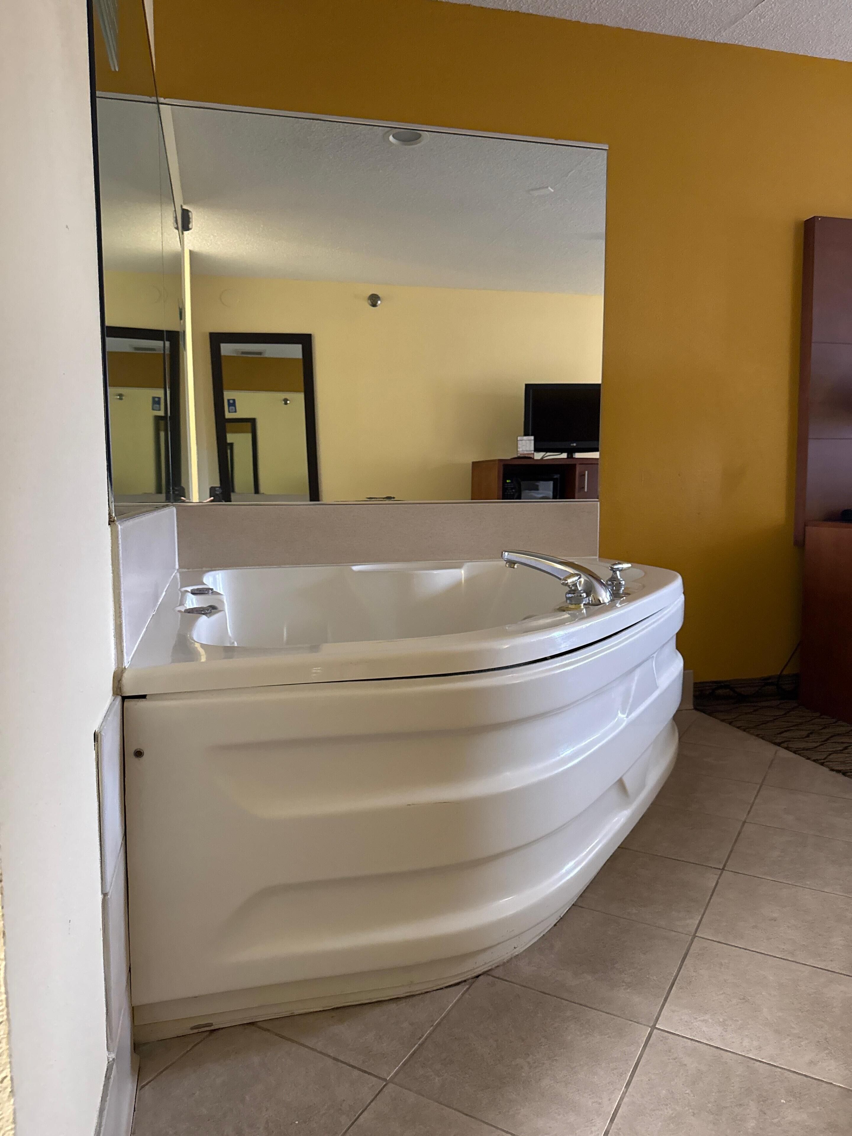 Uma casa de banho moderna com uma banheira branca grande, um espelho em cima e uma parede amarela.
