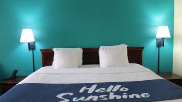 Uma cama com manta estampada com a frase 'Hello Sunshine', paredes verde-água e duas luminárias de cabeceira.