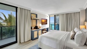 Quarto de hotel com uma cama grande, uma escrivaninha com computador, televisão e vista para o oceano.