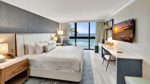 Quarto de hotel com uma cama grande, mesas de cabeceira, uma escrivaninha e vista para o oceano.