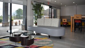 Um lobby moderno com um sofá curvo, mesa de centro de vidro e um tapete colorido.