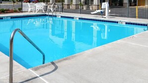 Piscina retangular com escada de metal, rodeada por um deck de concreto.