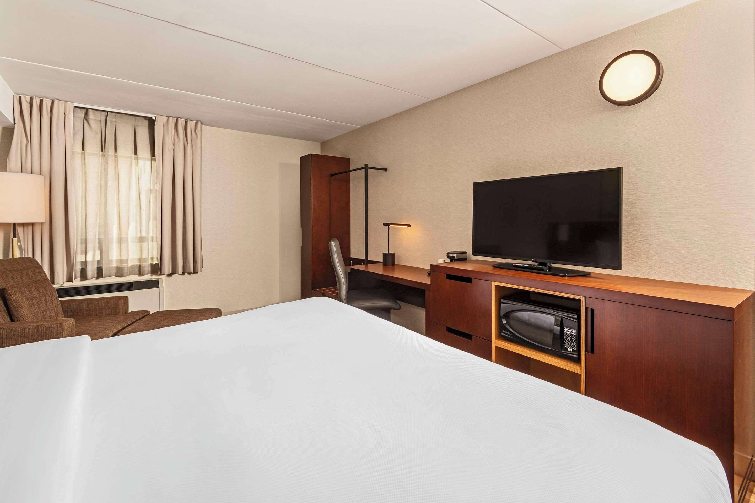 Quarto de hotel com uma cama grande, uma mesa com televisão, uma cadeira e um abajur.