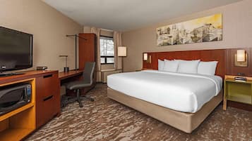 Quarto de hotel com uma cama grande, uma escrivaninha, uma televisão, micro-ondas e uma cadeira.