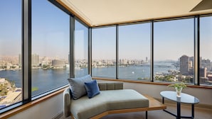 Quarto moderno com sofá curvo, uma mesinha e janelas amplas com vista para a cidade.