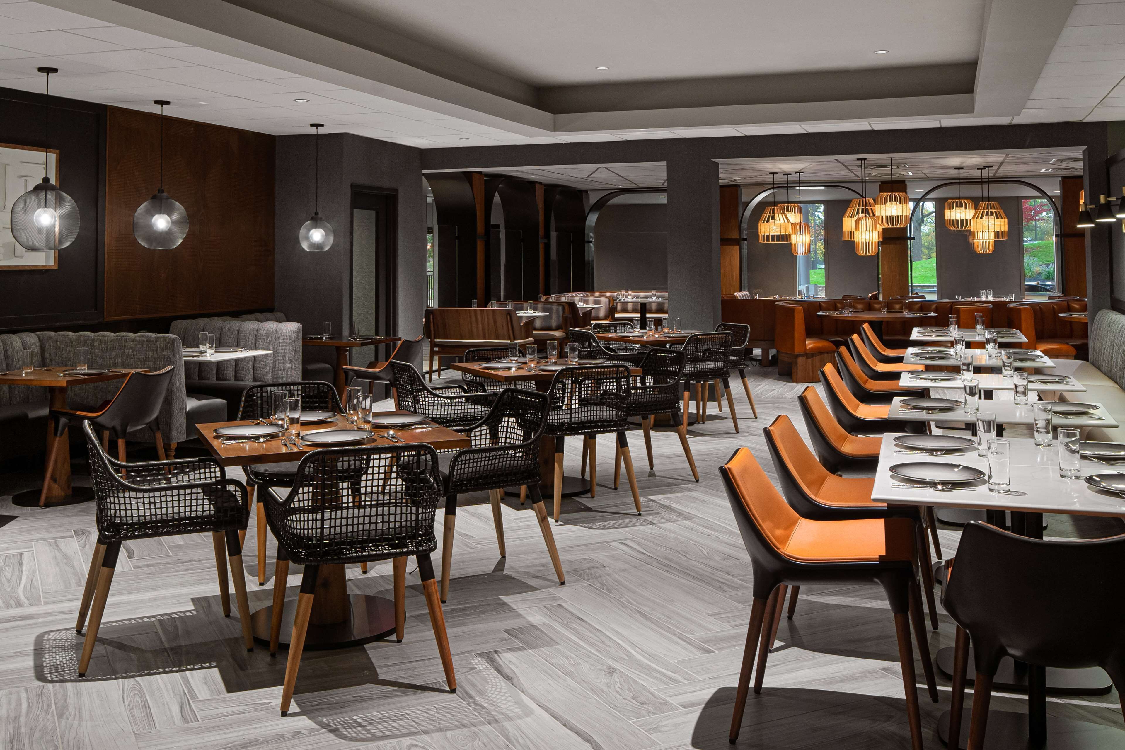 Restaurante moderno com uma combinação de assentos em cabines e mesas, piso de madeira e iluminação pendente.