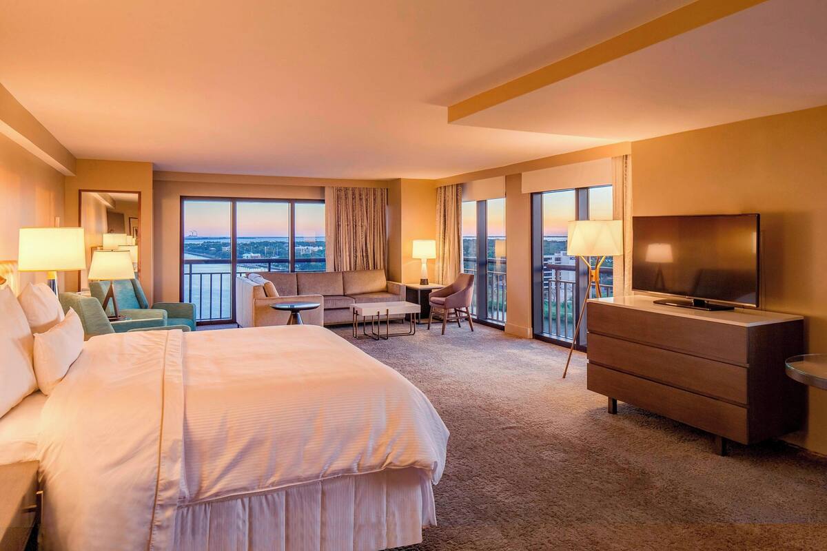 Quarto de hotel com uma cama grande, televisão, escrivaninha e varanda com vista.