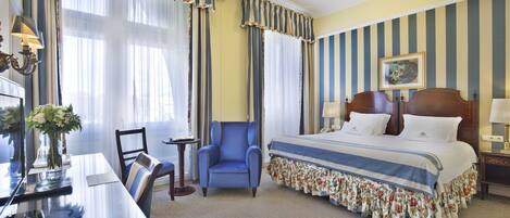 Quarto de hotel com uma cama grande, uma escrivaninha com telefone, uma cadeira e uma mesa pequena.