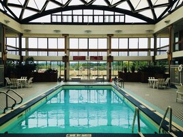 Piscina interna com sinalização clara das regras, várias áreas de estar e vista para o exterior através de grandes janelas.