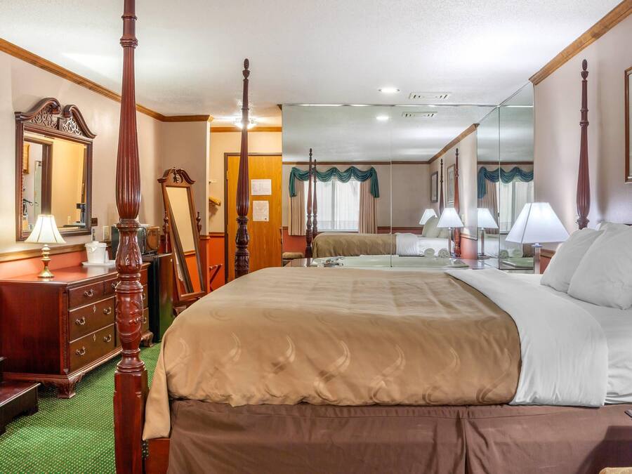 Quarto de hotel com cama de dossel, cômoda, espelho e janela com cortinas.
