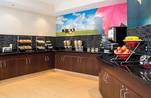 Cozinha moderna com bancada preta, armários de madeira e um mural com tema rural.