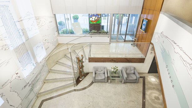 Interior moderno com piso de mármore, escada, assentos cinzas e uma janela grande com vista para o exterior.