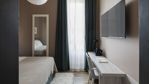 Quarto de hotel moderno com cama, escrivaninha, televisão e uma grande janela com cortinas.