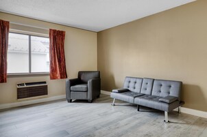 Uma sala de estar com um sofá cinzento, uma poltrona preta e uma janela com cortinas vermelhas.