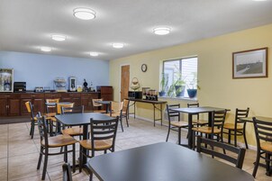 Uma área de refeições com várias mesas e cadeiras, uma cozinha com eletrodomésticos e uma janela com vista.