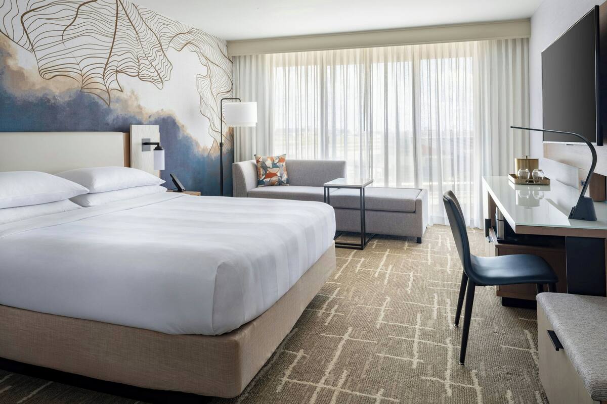 Quarto de hotel com uma cama grande, uma escrivaninha, uma cadeira, um sofá e uma televisão.