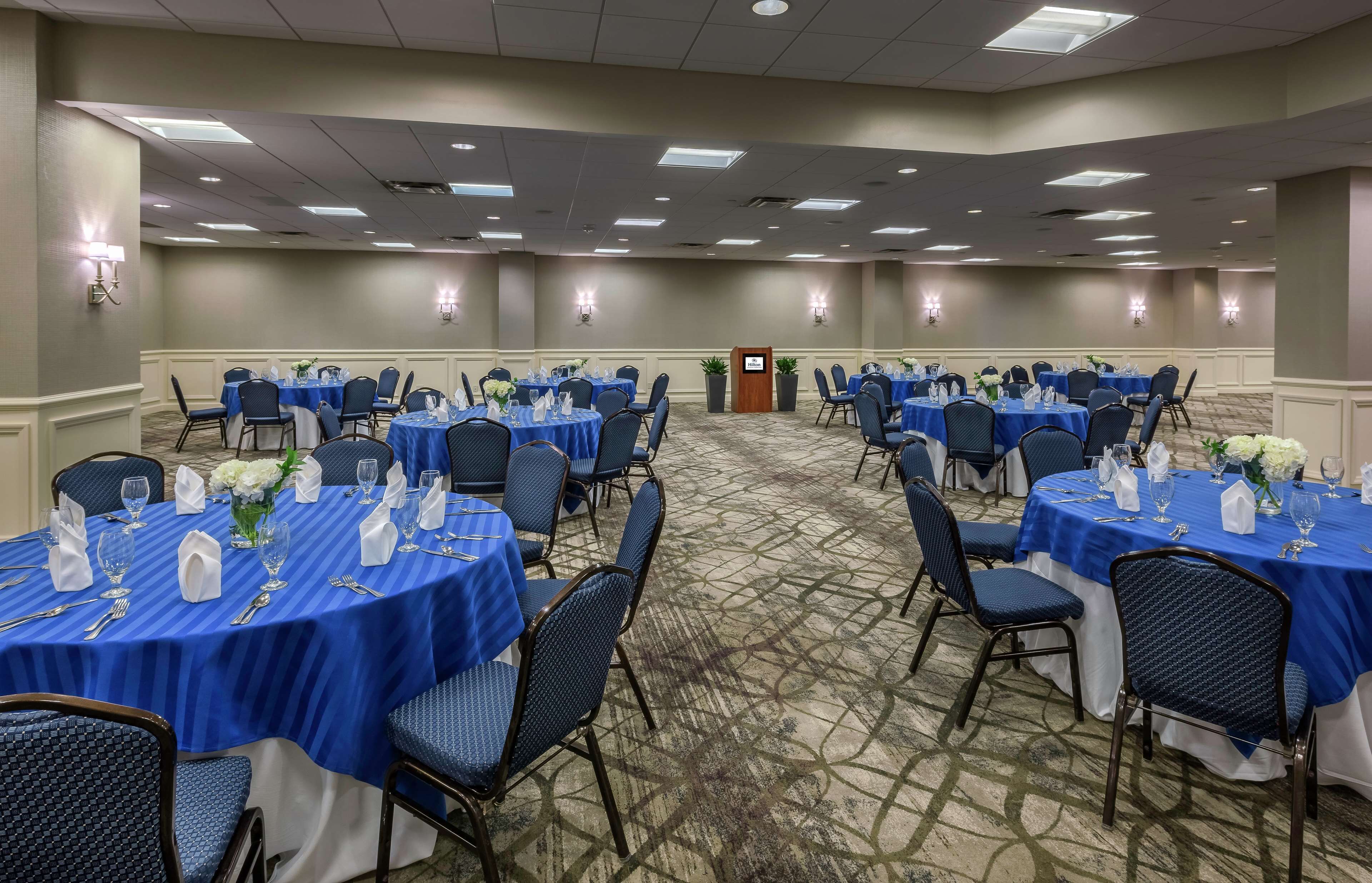 Sala de conferência com mesas redondas, toalhas azuis e cadeiras.