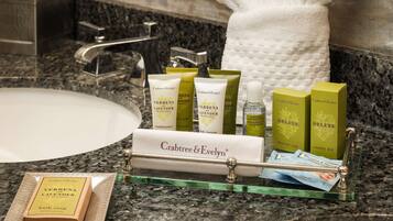 Uma toucador de banheiro com bancada de mármore, pia e porta-sabonete de vidro contendo diversos produtos Crabtree & Evelyn.