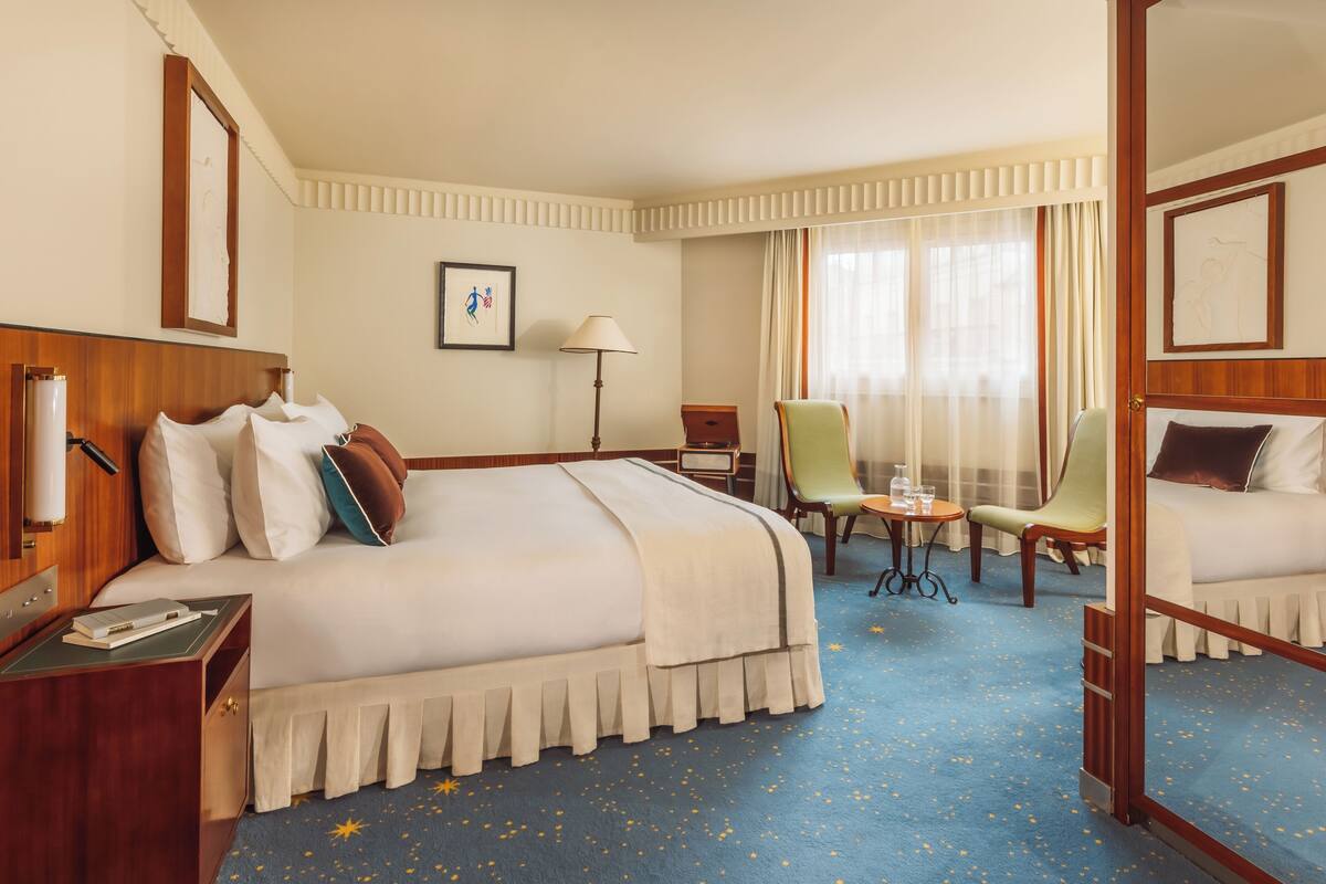 Quarto de hotel com uma cama grande, uma escrivaninha, uma cadeira, uma mesa pequena e um espelho.