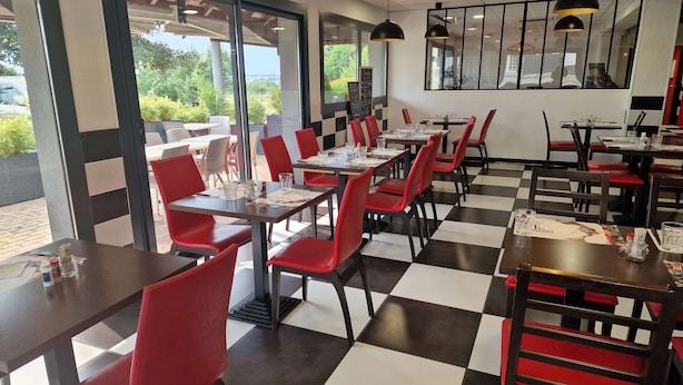 Restaurante com chão xadrez, cadeiras vermelhas e mesas postas para refeições.