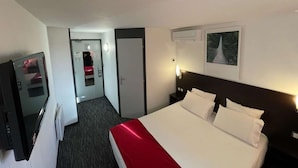Quarto de hotel com cama, televisão, porta e ar condicionado fixado na parede.