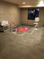 Uma área de piscina com piso ladrilhado, escada para piscina, um banco e um porta-toalhas.
