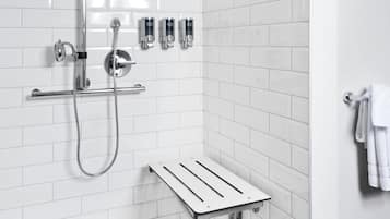 Casa de banho moderna com paredes revestidas a azulejos brancos, chuveiro manual, pulverizador de mão e um porta-toalhas com uma toalha dobrada.