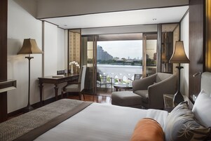 Quarto de hotel com uma cama grande, uma escrivaninha, uma cadeira e vista para a cidade através de uma porta de vidro.
