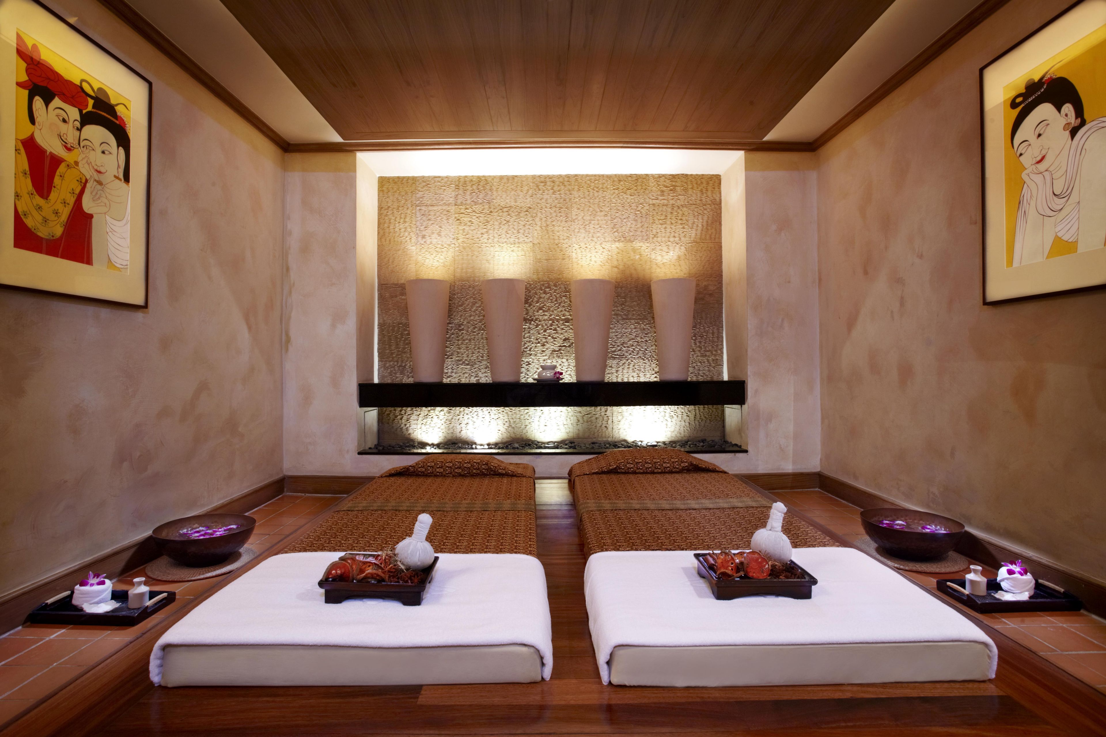 Um salão de spa com duas macas de massagem, um recurso de água embutido na parede e obras de arte emolduradas nas paredes.