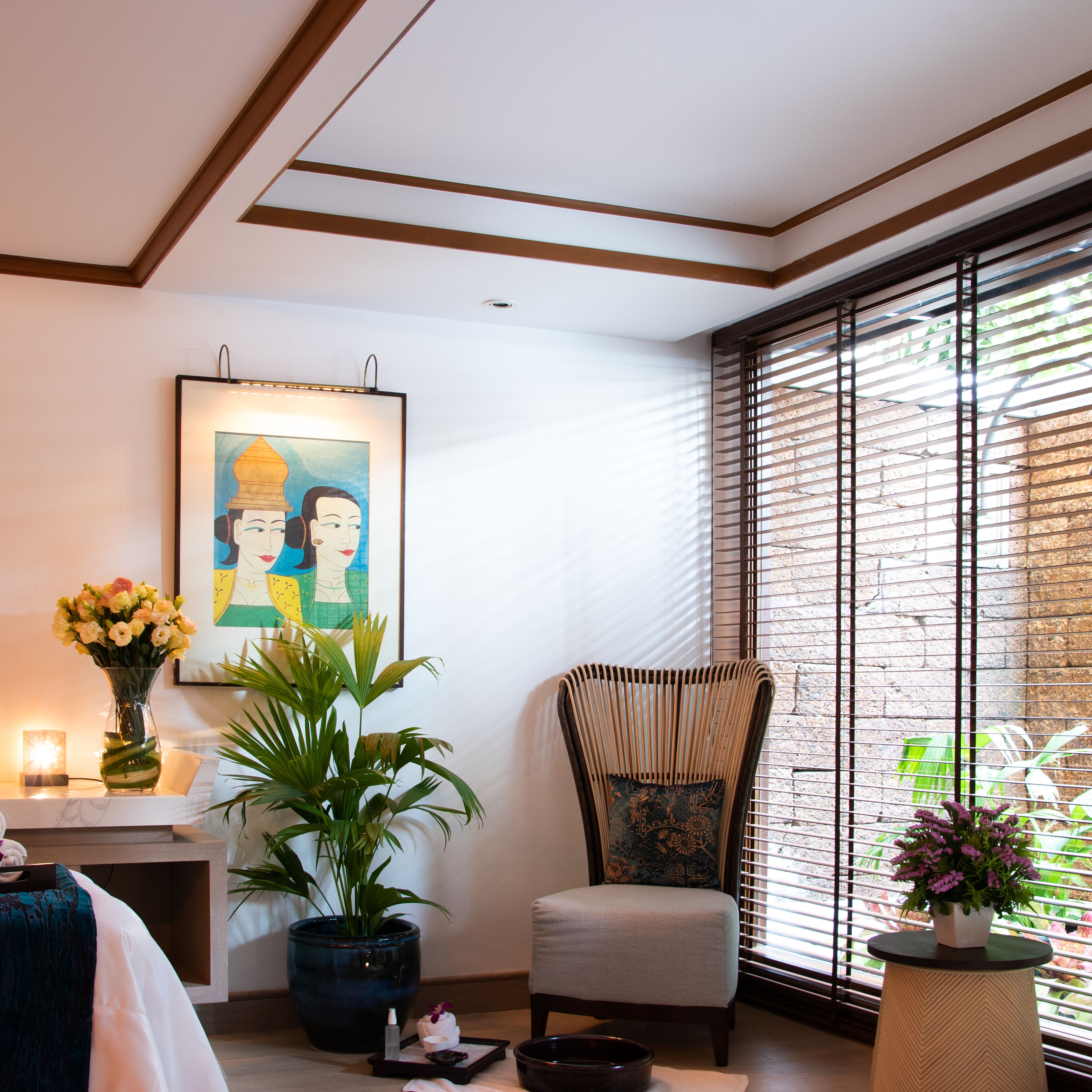 Quarto com uma janela grande, uma cadeira, uma mesa com um vaso de flores, um quadro emoldurado e uma planta em vaso.