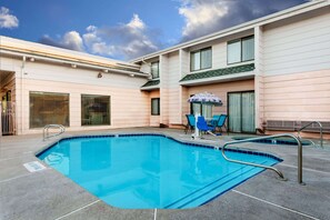 Piscina com borda em azulejo, área de estar com cadeiras e espaço coberto com guarda-sol.