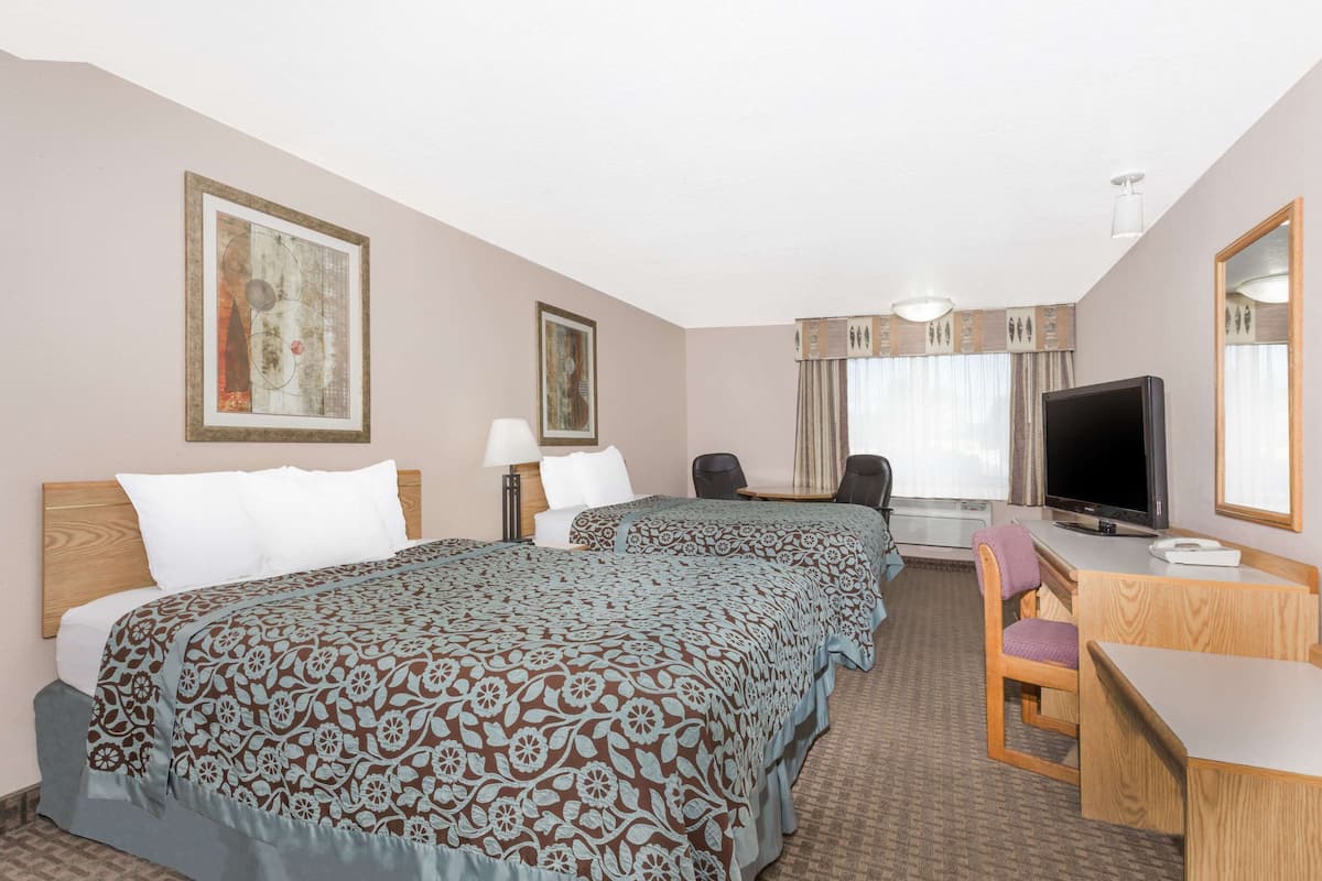 Quarto de hotel com duas camas, uma escrivaninha, uma cadeira, televisão e obras de arte nas paredes.