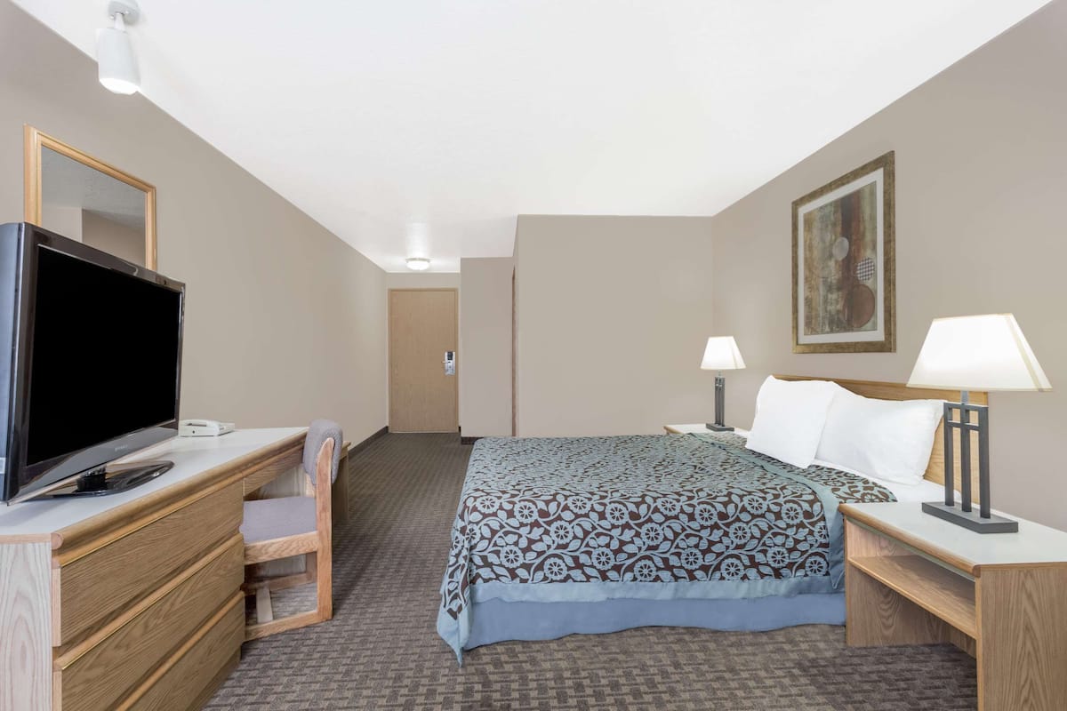 Quarto de hotel com cama, secretária com televisão, cadeira, mesa de cabeceira com luminárias e porta para outro quarto.