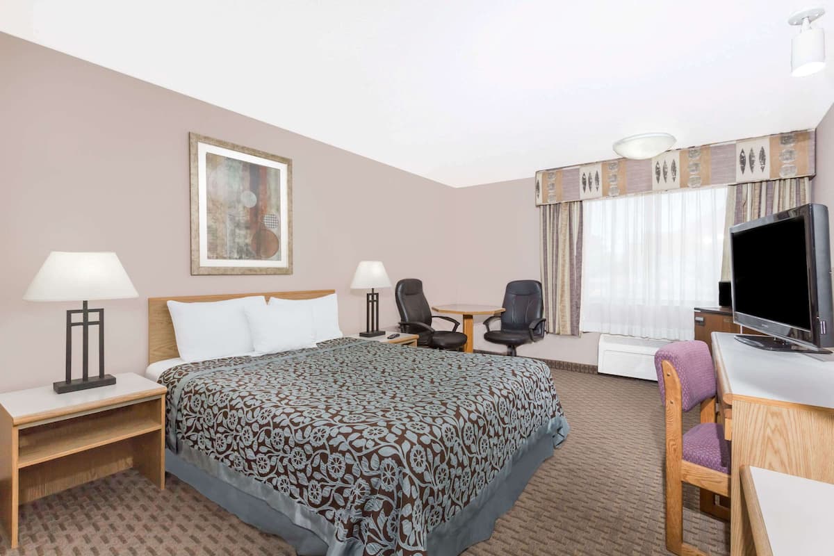 Quarto de hotel com uma cama grande, duas mesas de cabeceira com abajures, uma escrivaninha com cadeira, uma televisão e uma janela com cortinas.