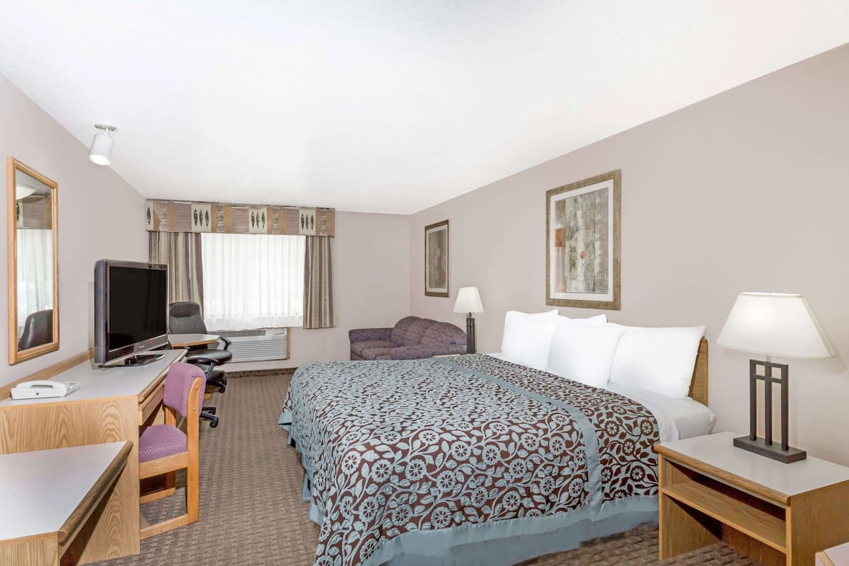 Quarto de hotel com cama, secretária com computador, cadeira, televisão e luminária.