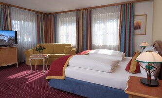 Quarto de hotel com cama, sofá, televisão e cortinas.