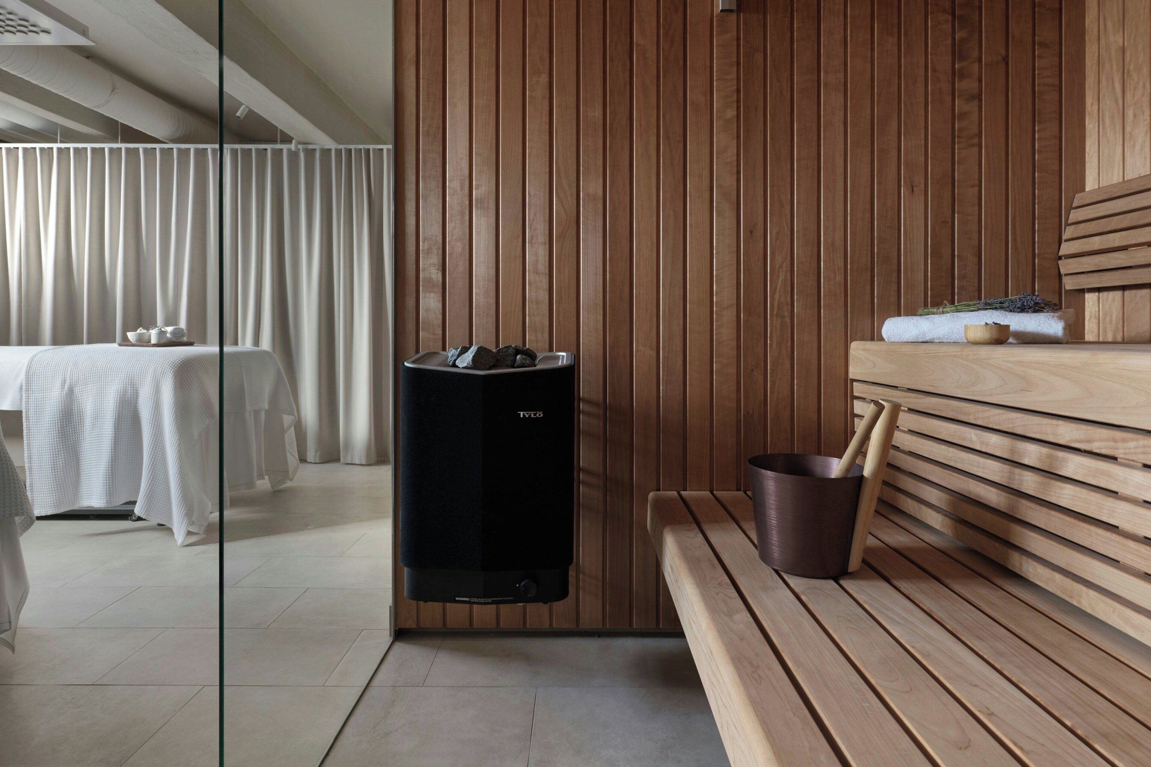 Uma sauna moderna com um banco de madeira, um aquecedor de sauna preto e um balde de madeira.