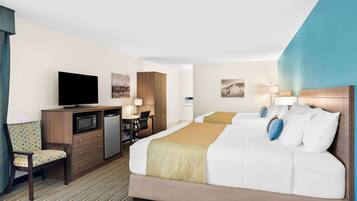 Quarto de hotel com cama, mesa de trabalho com televisão, cadeira, guarda-roupa e micro-ondas.