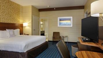 Quarto de hotel com cama, escrivaninha, cadeira, televisão e janela com vista.