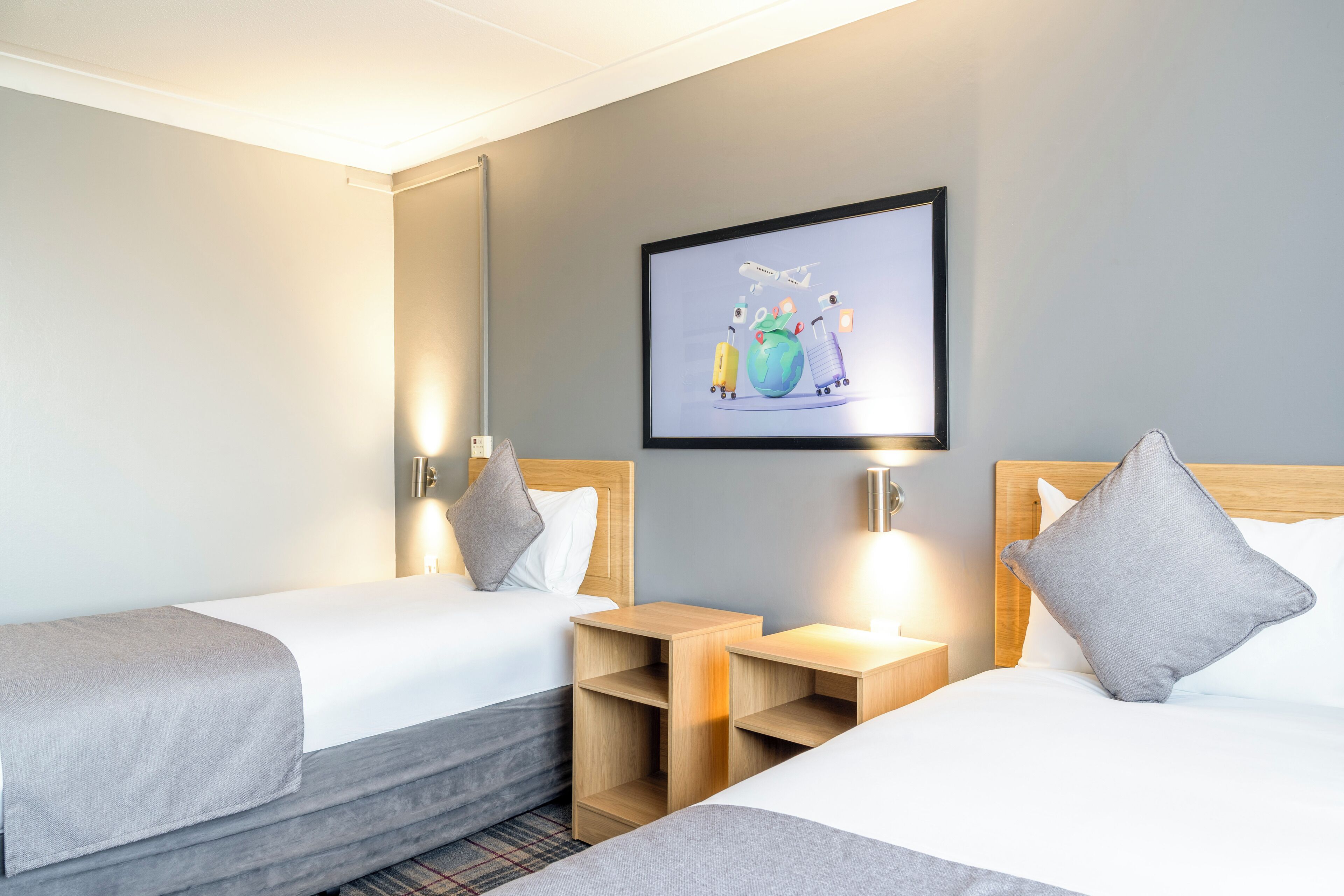 Quarto de hotel com duas camas, uma TV de tela plana na parede e mesas de cabeceira com luminárias.