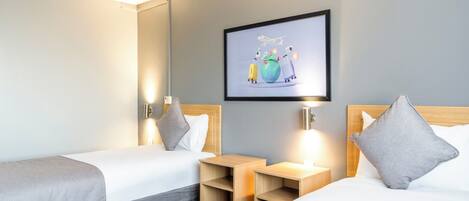 Quarto de hotel com duas camas, uma TV de tela plana na parede e mesas de cabeceira com luminárias.
